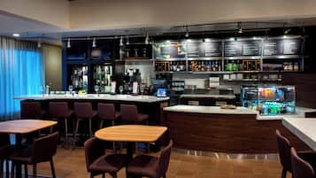 Zona de bar com lugares e balcão exibindo diversas bebidas e um cardápio.