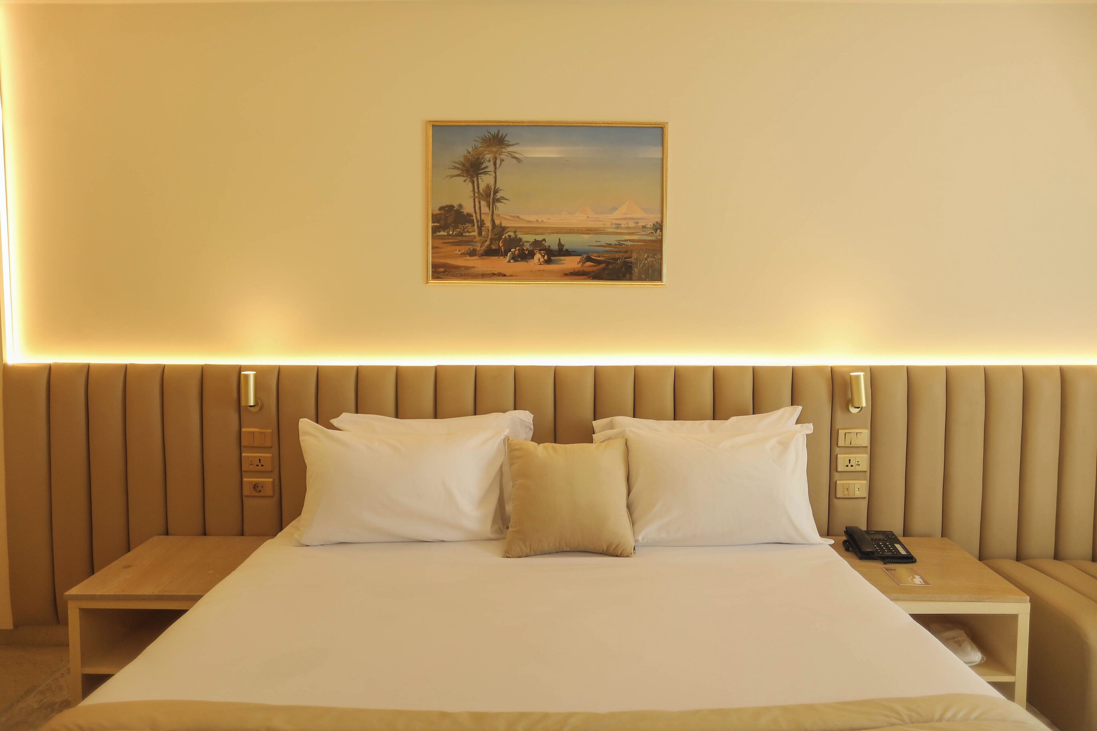Quarto de hotel com cama, mesas de cabeceira, um quadro e um criado-mudo.