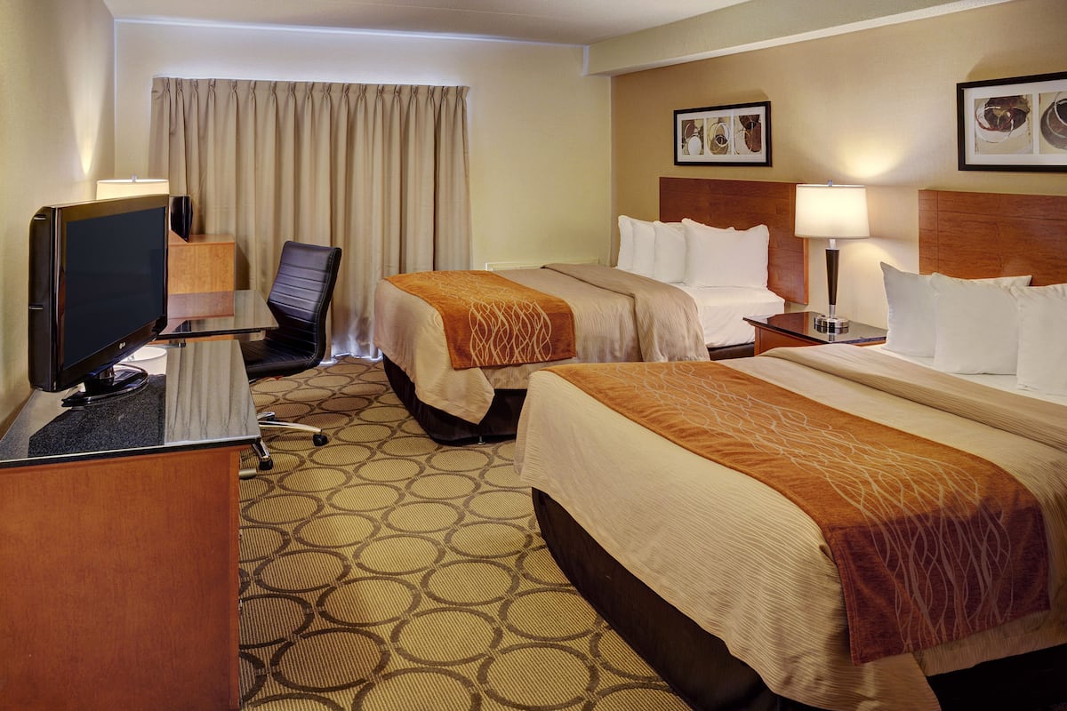 Quarto de hotel com duas camas, uma escrivaninha com computador, uma cadeira e uma televisão.