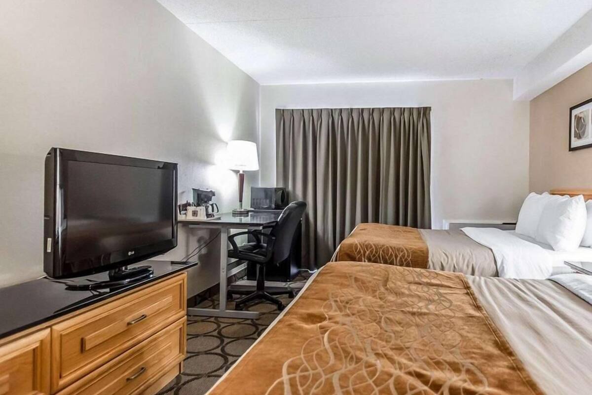 Quarto de hotel com televisão, escrivaninha, cadeira, duas camas e janela com cortinas.