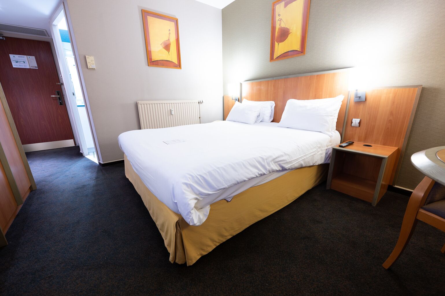 Quarto de hotel com uma cama grande, duas mesas de cabeceira, uma cadeira e obras de arte nas paredes.