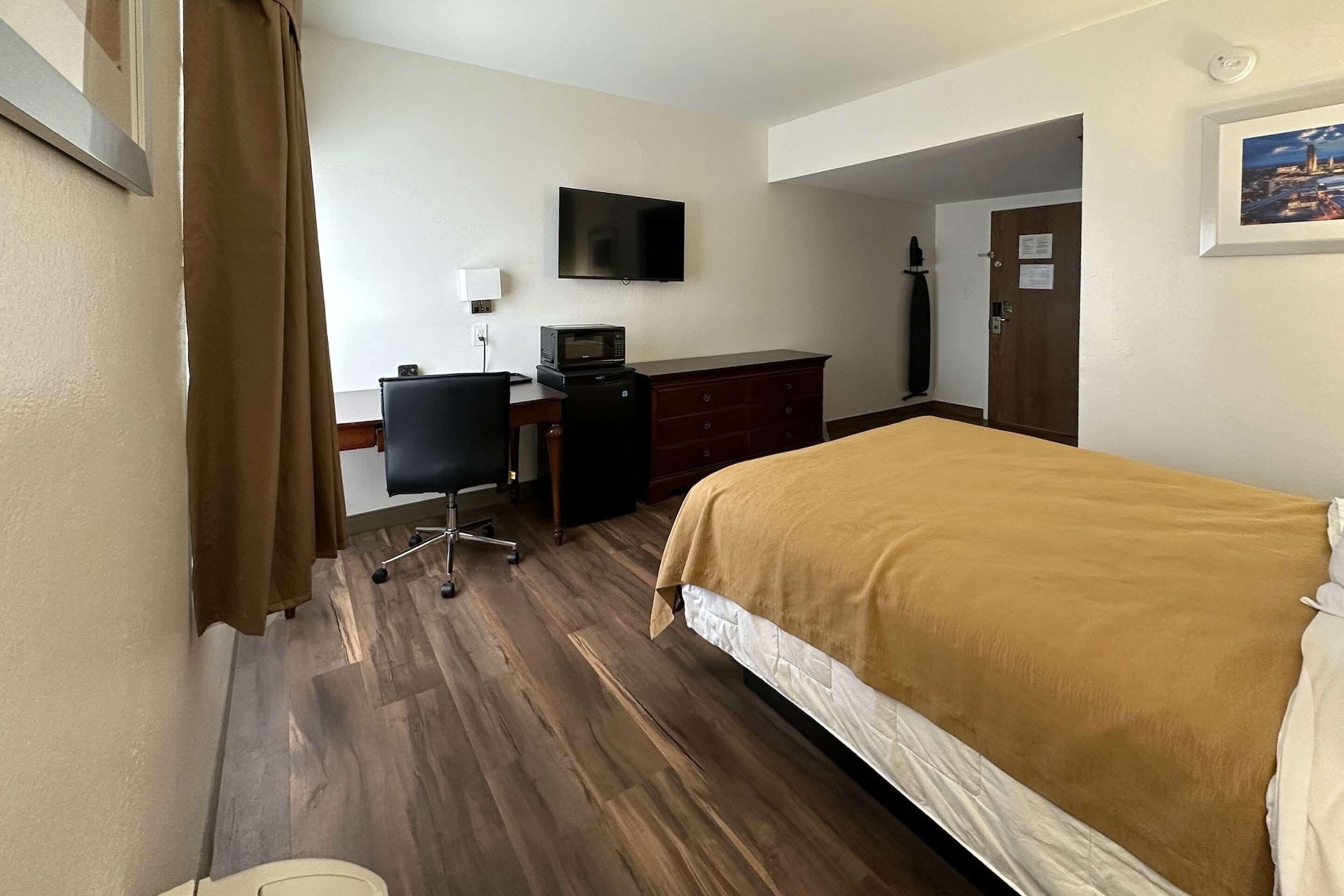Quarto de hotel com uma cama, uma escrivaninha com computador, televisão e cómoda.
