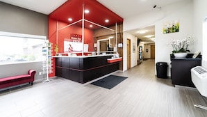Uma área de recepção com balcão vermelho e preto, um banco e uma planta.