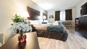 Quarto de hotel com cama, mesa de cabeceira, abajur e televisão.
