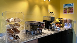 Uma cozinha compacta com máquina de panquecas sem contato, cafeteira e diversos alimentos sobre o balcão.