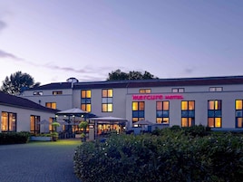 Hotel com fachada moderna, entrada bem iluminada e área externa com mesas.