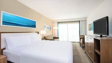 Quarto de hotel com uma cama grande, televisão, escrivaninha com cadeira e janela com cortinas.