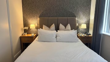 Quarto de hotel com uma cama grande, duas mesas de cabeceira com luminárias, parede texturizada e janela com cortinas.