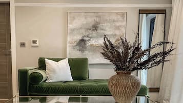 Um sofá verde com almofadas brancas, um vaso decorativo com plantas secas e uma grande pintura abstrata na parede.