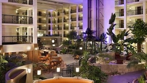 Um átrio de hotel com vários andares, varandas, plantas em vasos e áreas de estar.