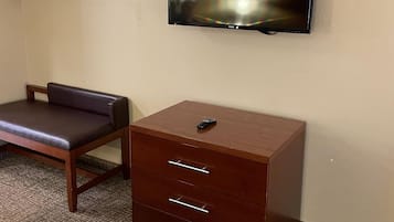 Quarto de hotel com uma cama de solteiro, mesa de cabeceira de madeira, televisão fixada na parede e controle remoto na mesa.