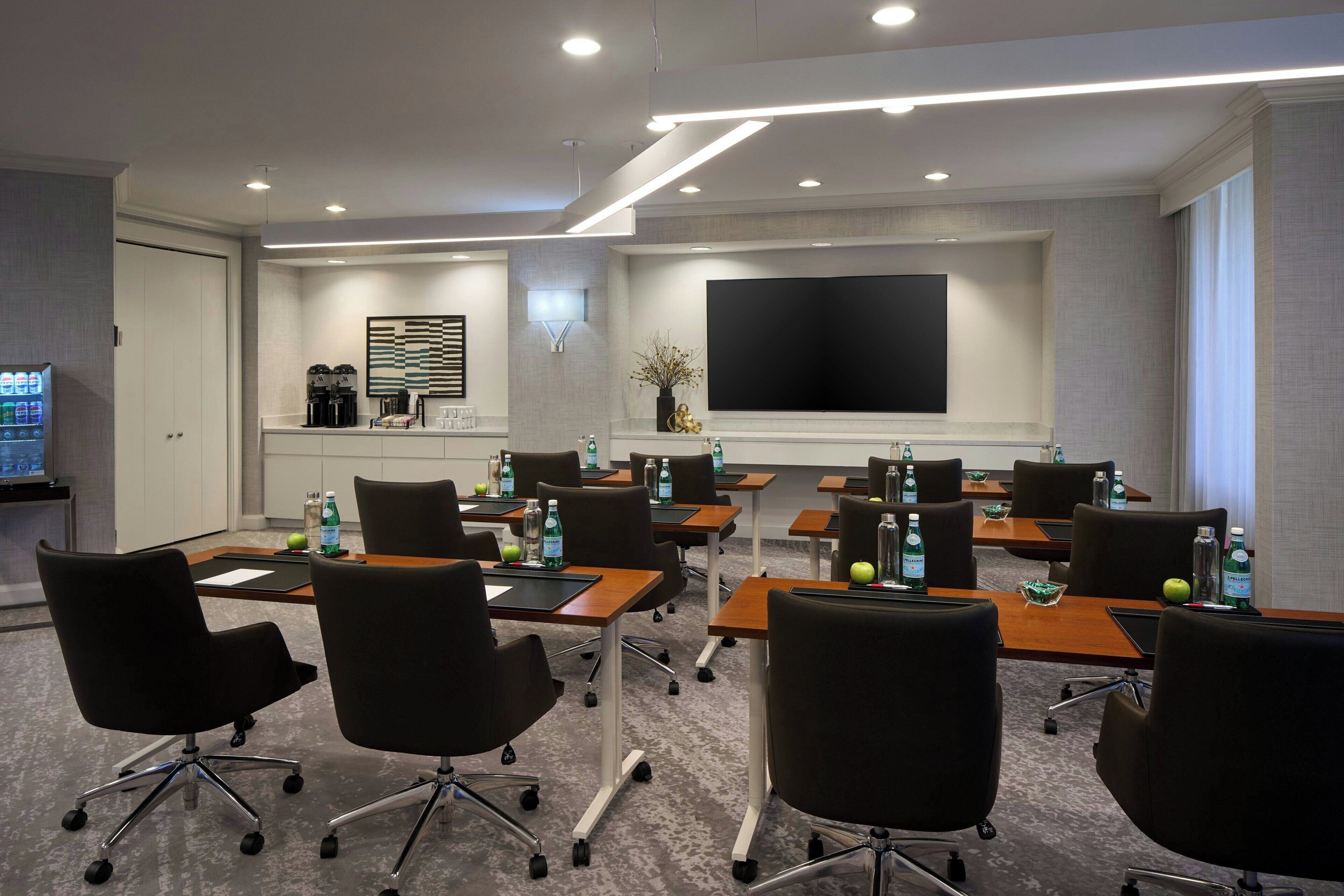 Uma sala de conferências com mesas, cadeiras, uma grande televisão de tela plana e um espaço para café.