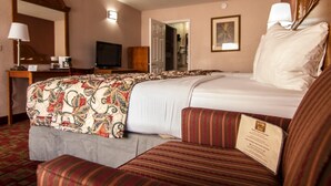 Quarto de hotel com uma cama, televisão, escrivaninha com luminária e uma cadeira.