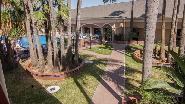 Um resort com área de piscina, palmeiras e um caminho que leva ao edifício.