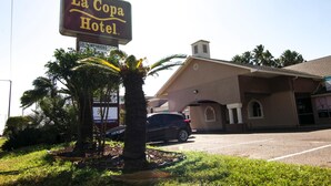 Placa do Hotel La Copa, com um estacionamento e palmeiras à frente.