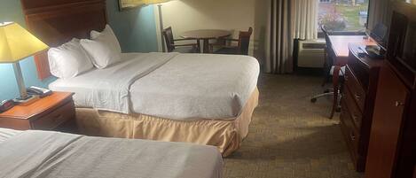Quarto de hotel com duas camas, uma mesa com cadeira, televisão e janela com vista exterior.