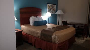 Quarto de hotel com uma cama grande, uma escrivaninha, uma cadeira e um abajur.