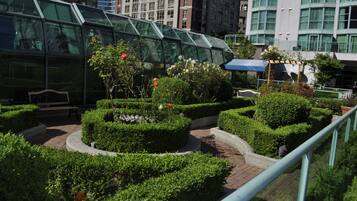Um jardim urbano moderno com sebes bem aparadas, um banco e uma estrutura de vidro.