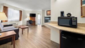 Quarto de hotel com sofá, mesa pequena, micro-ondas, cafeteira, televisão e lareira.