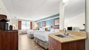 Quarto de hotel com duas camas, cozinha compacta, um espelho grande e uma televisão.