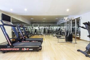 Uma academia com esteiras, máquinas de musculação e espelhos.