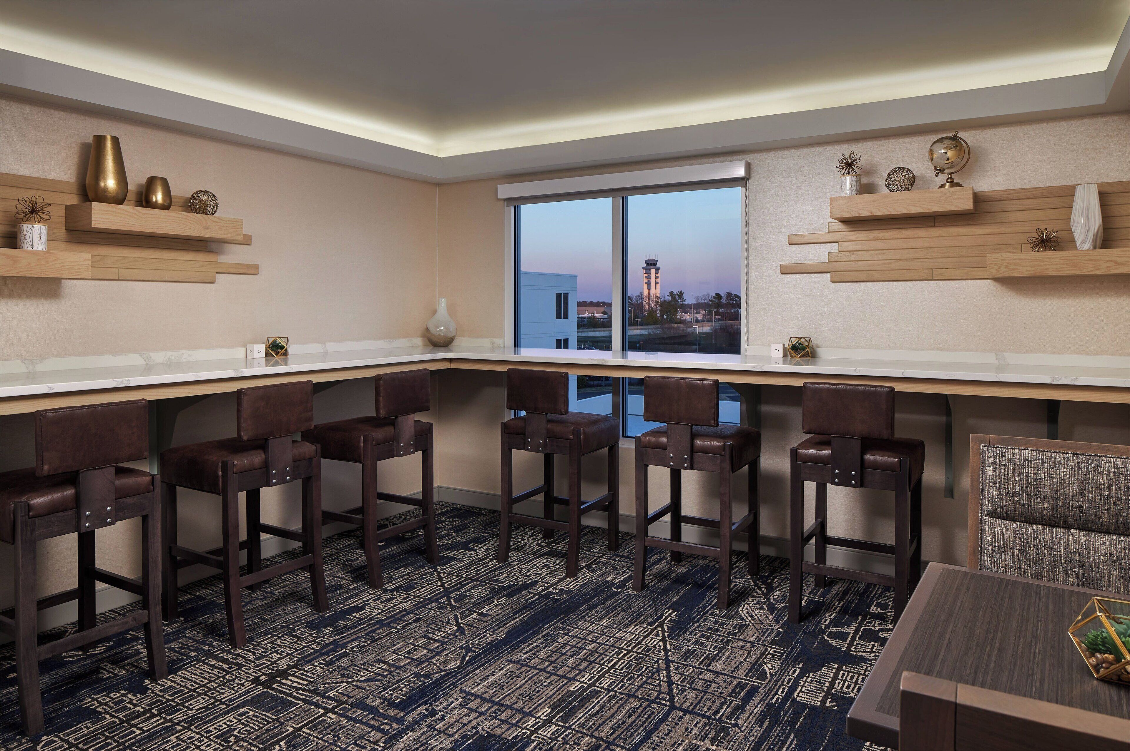 Cozinha moderna com uma grande janela, banquetas de bar e prateleiras de madeira com objetos decorativos.
