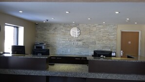 Balcão de recepção de hotel com parede de pedra ao fundo, um computador Dell e uma placa com o dizer 'Comfort Inn'.