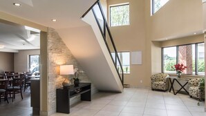Um interior espaçoso com teto alto, parede de pedra decorativa, escada e área de estar com mesa e cadeiras.