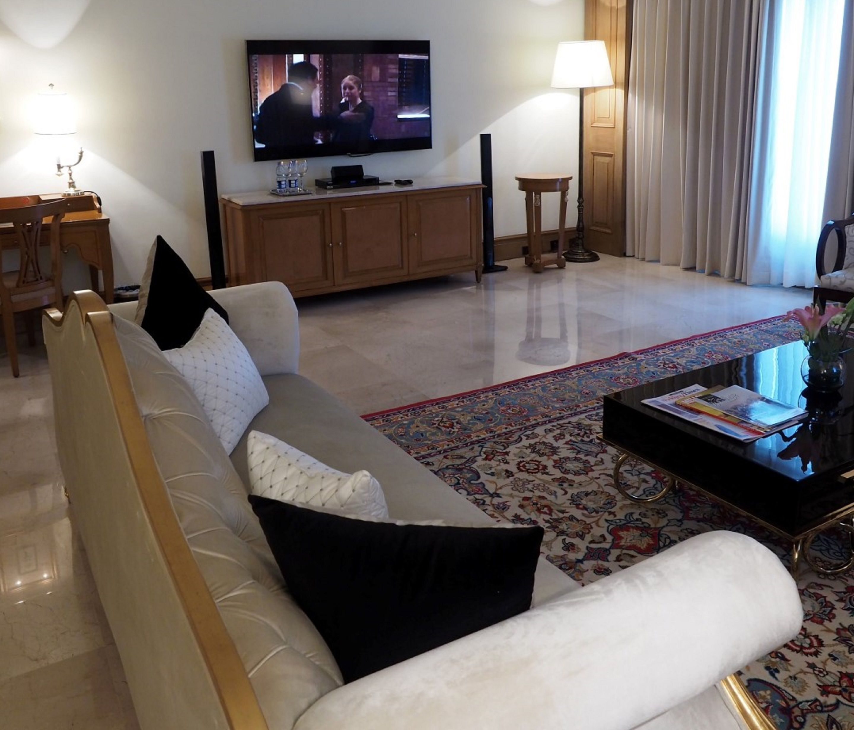 Uma sala de estar com sofá, mesa de centro, televisão e tapete estampado.