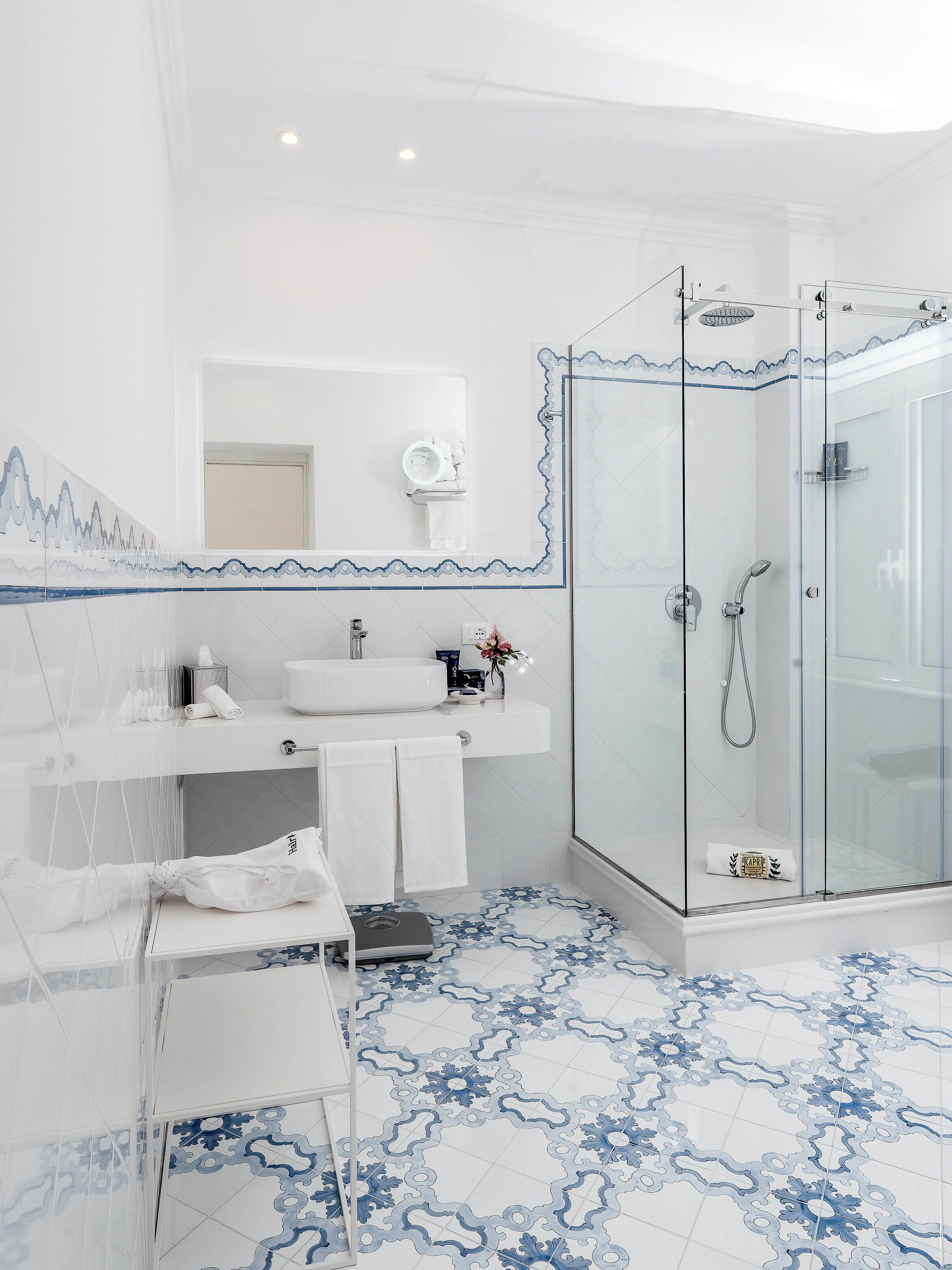 Uma casa de banho moderna com chuveiro envidraçado, lavatório branco e chão estampado.