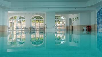 Piscina interna com água cristalina, janelas em arco e cadeira do salva-vidas.