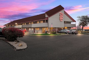 Um Red Roof Inn com estrutura de dois andares, estacionamento e uma bandeira americana.