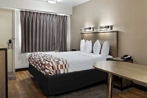 Quarto de hotel com cama, escrivaninha, telefone e janela com cortinas.