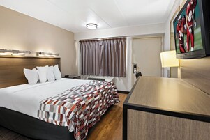 Quarto de hotel com cama, mesa de cabeceira, abajur e um quadro na parede.