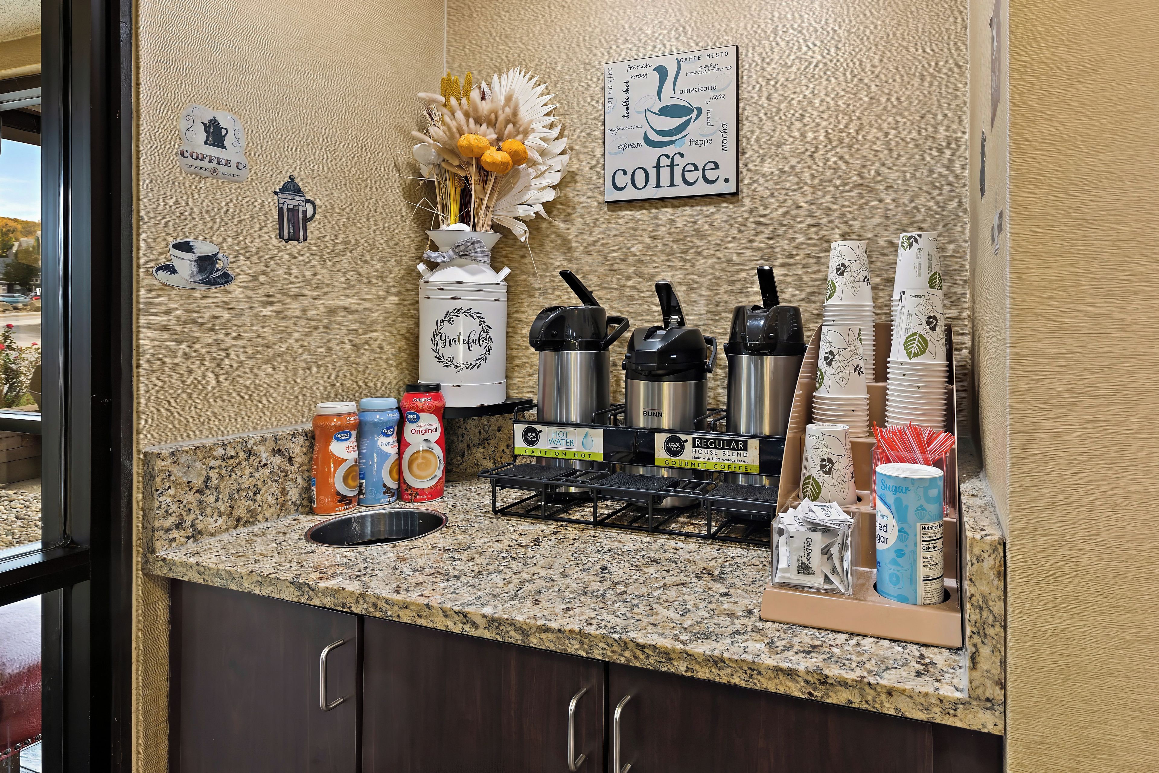 Estação de café com máquina de café, xícaras e um aviso que diz 'café'.
