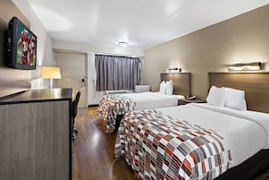 Quarto de hotel com duas camas, uma mesa, uma televisão e uma luminária.