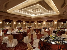 Uma sala de banquetes com mesas redondas, cadeiras e lustres.