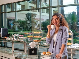 Mulher em um saguão de hotel com uma mesa de buffet exibindo diversos alimentos.