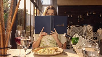 Uma pessoa sentada à mesa com um menu, copos de vinho e pratos de comida.