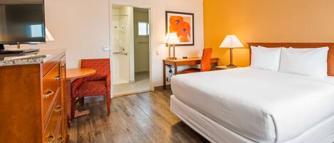 Quarto de hotel com cama, escrivaninha, cadeira, televisão e porta do banheiro.