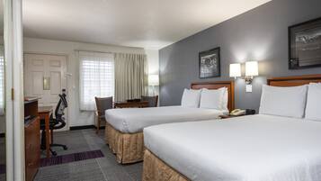 Quarto de hotel com duas camas, uma escrivaninha, uma cadeira e uma luminária de mesa.