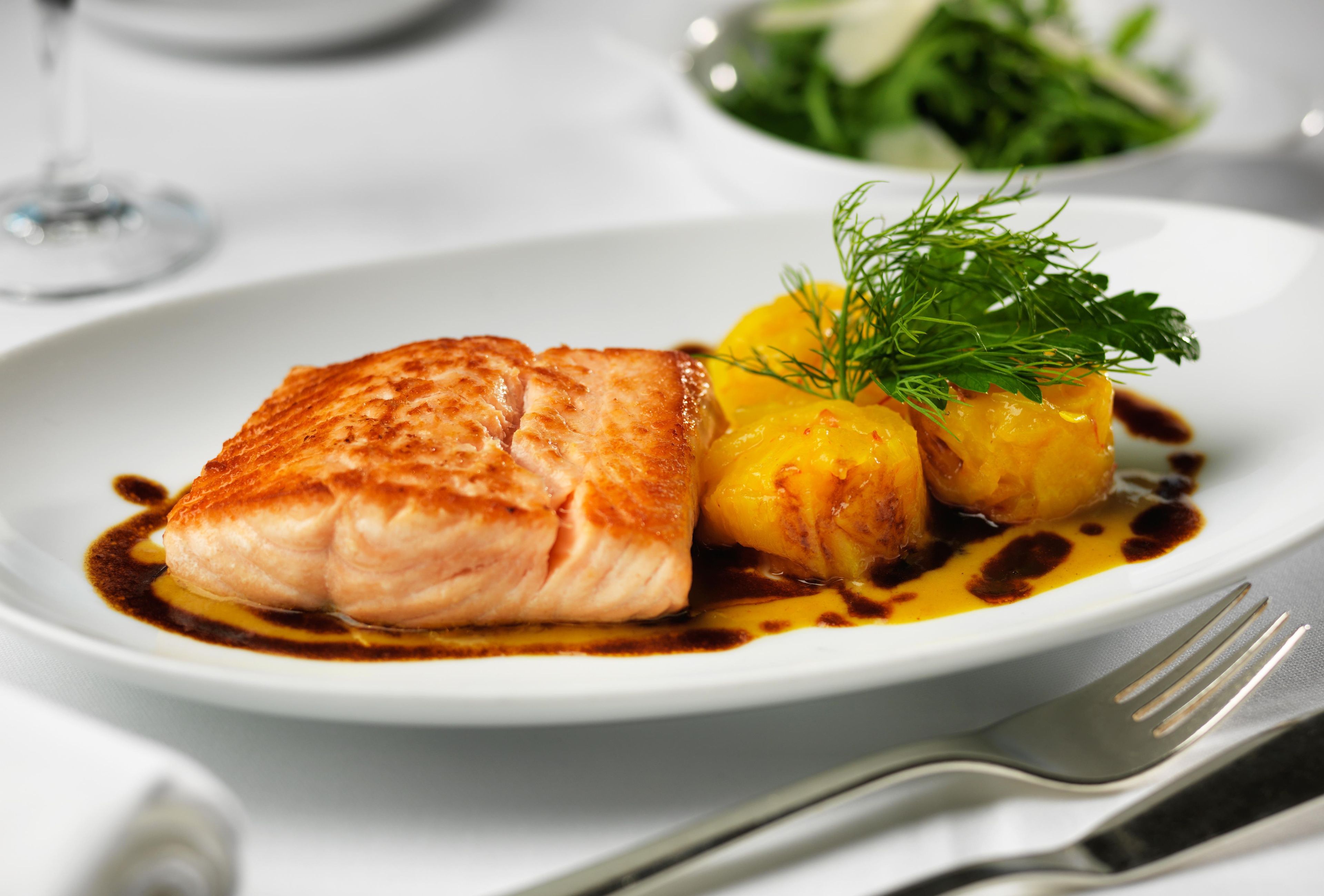Um prato com um pedaço de peixe cozido, um purê amarelo e um enfeite de ervas verdes.