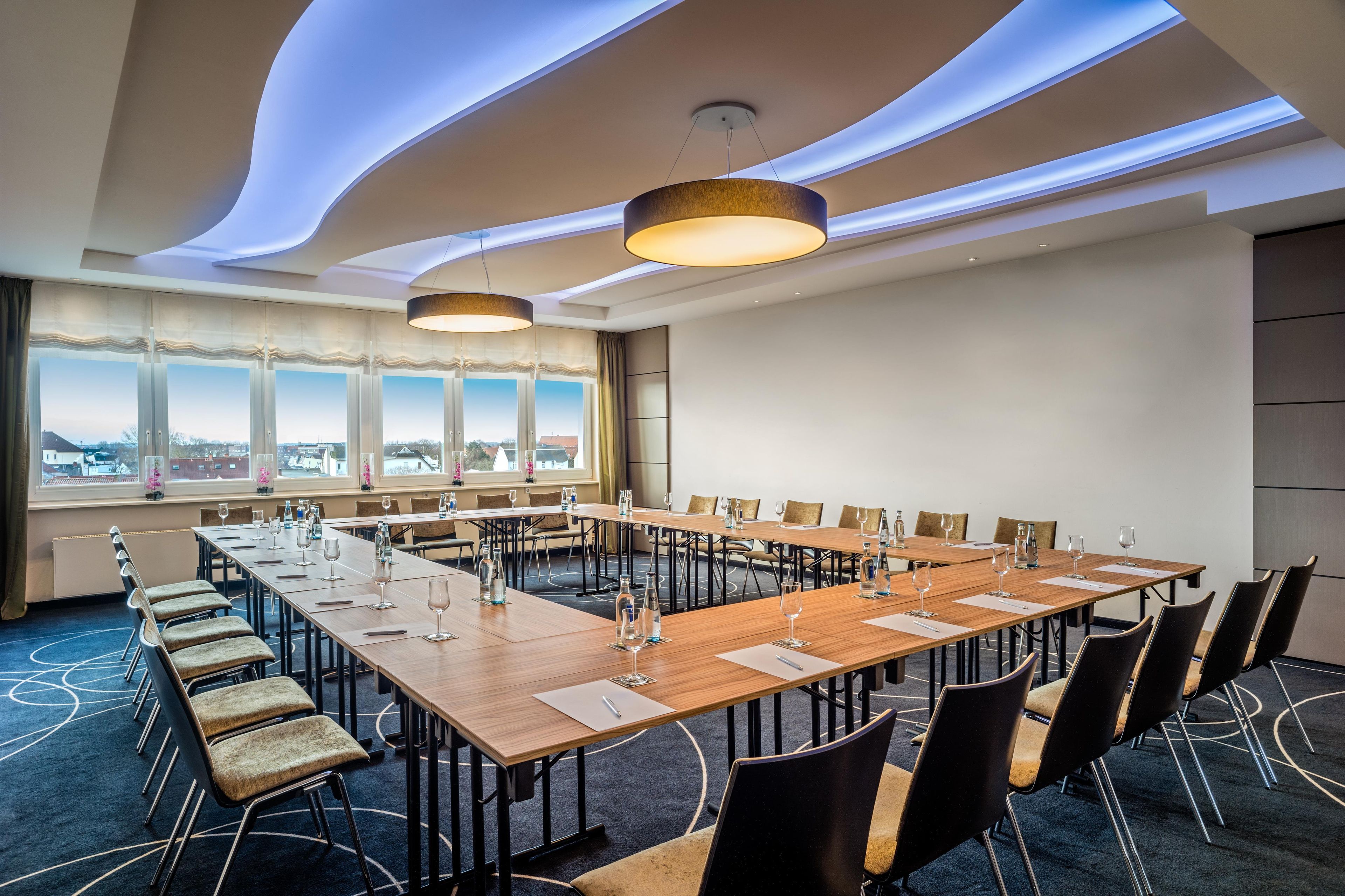 Sala de conferências com uma mesa comprida, cadeiras e grandes janelas com vista para a cidade.