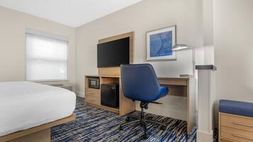 Quarto de hotel com cama, escrivaninha, cadeira, micro-ondas e um mapa emoldurado na parede.