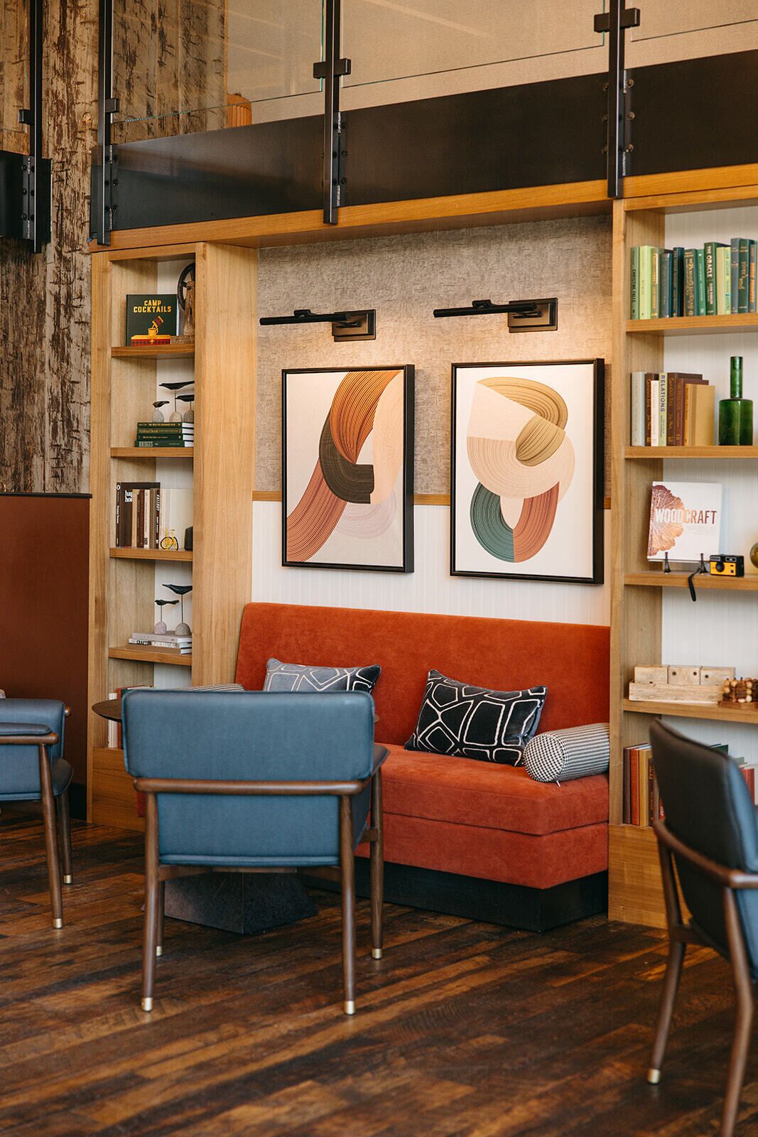Um espaço de estar acolhedor, com um sofá vermelho e cadeiras azuis, cercado por estantes de madeira e quadros abstratos.