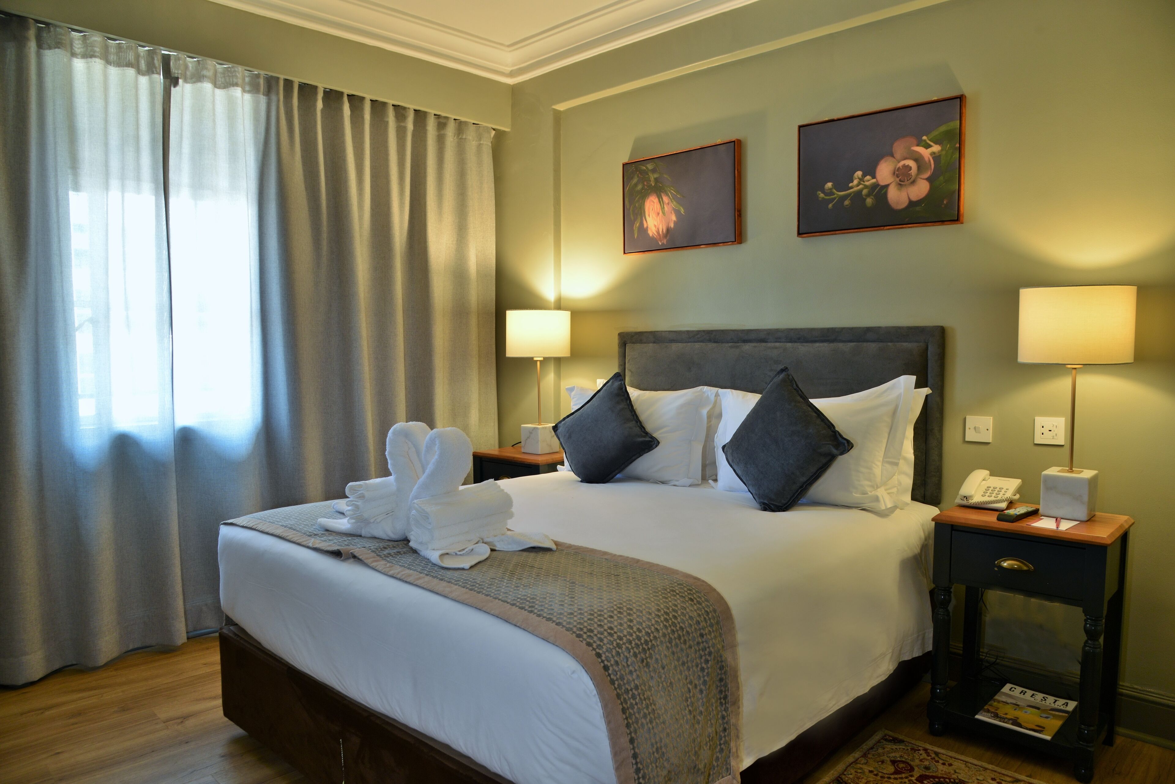 Quarto de hotel com uma cama grande, duas luminárias de cabeceira, uma mesa de cabeceira com um telefone e um controle remoto, e um quadro na parede.
