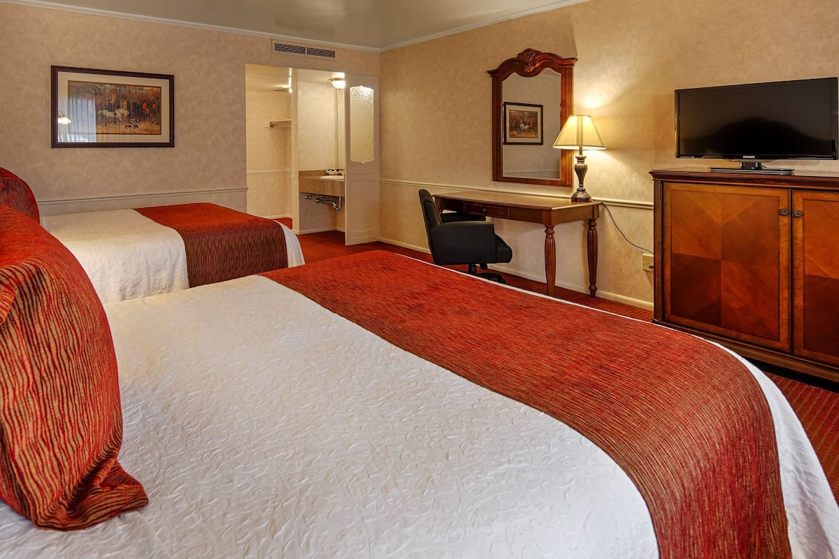 Quarto de hotel com duas camas, uma escrivaninha, uma televisão e um espelho.