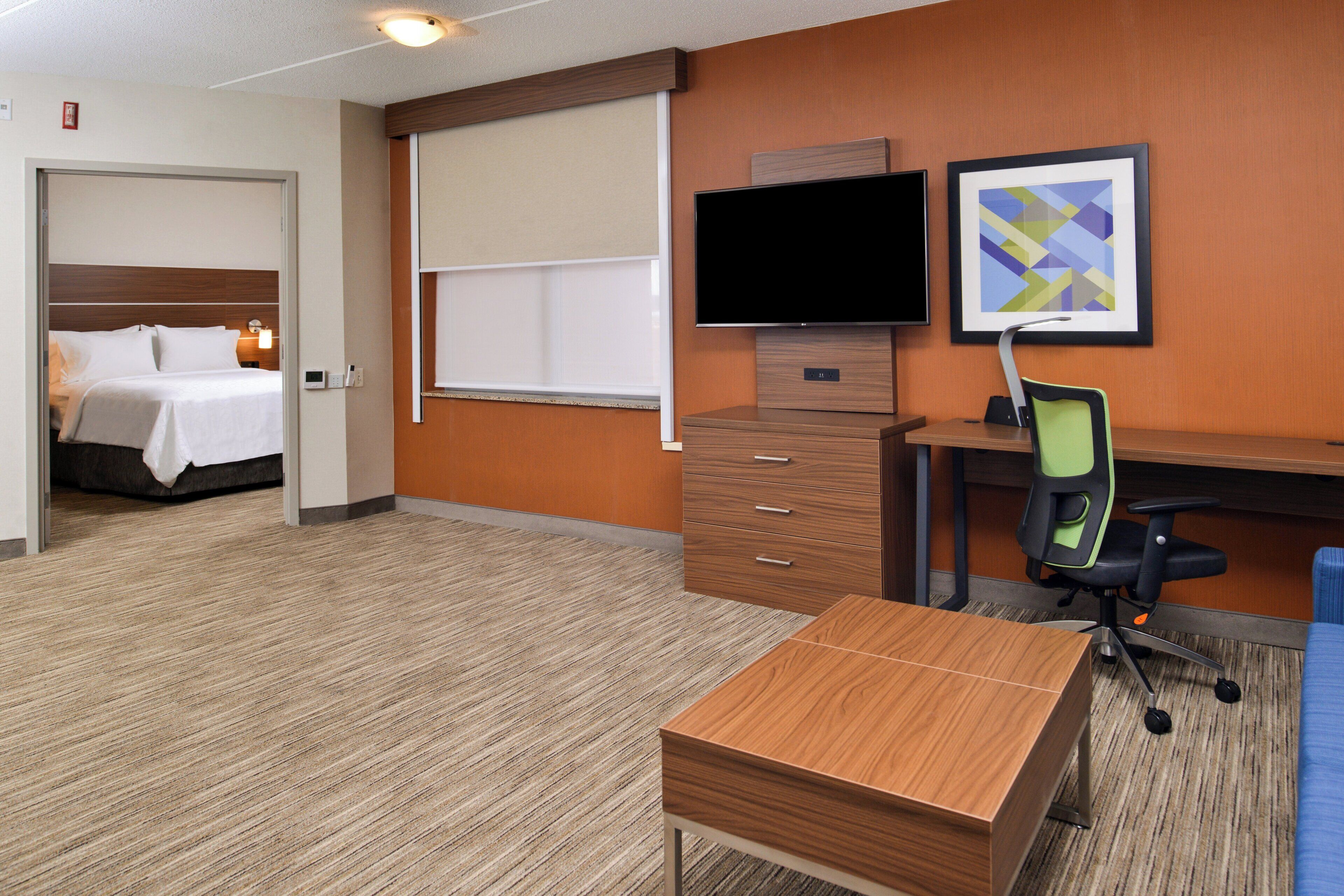 Quarto de hotel com cama, escrivaninha, cadeira, televisão e quadro na parede.