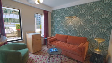 Quarto com sofá, poltrona, mesa pequena, luminária, janela com cortinas e parede estampada.