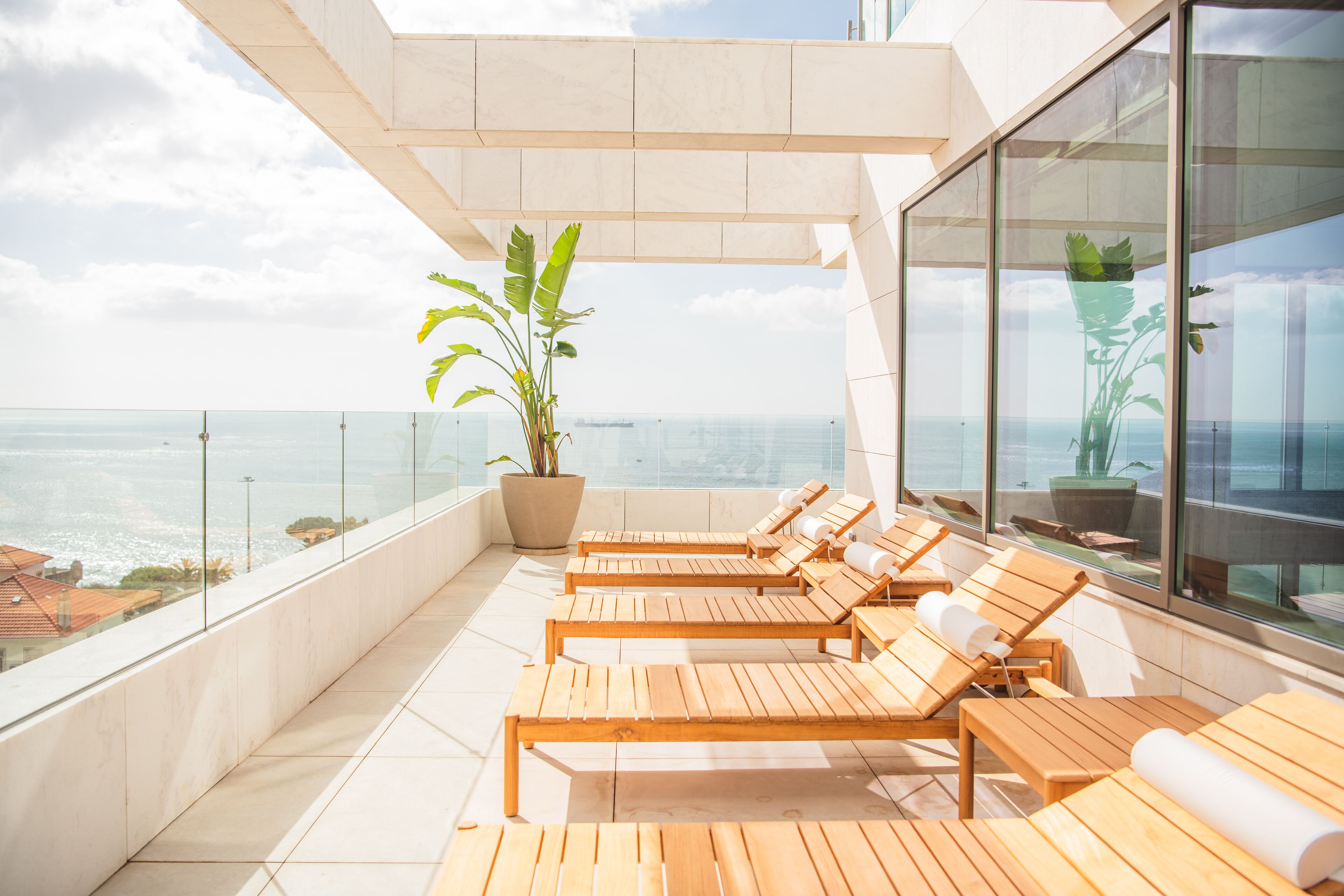 Terraço no telhado com cadeiras de lounge de madeira, plantas em vasos e vista para o oceano.